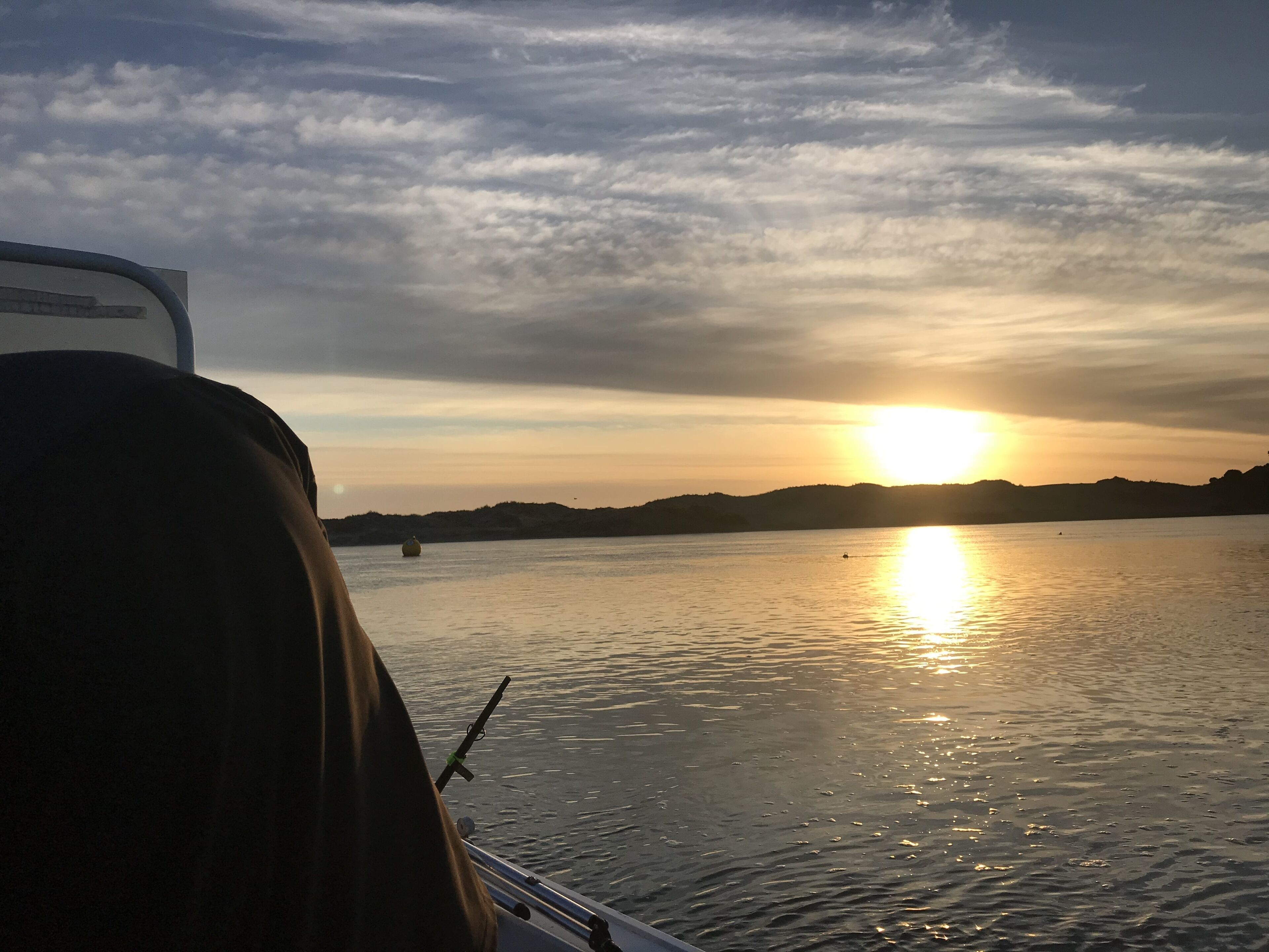 Um barco com vara de pesca e um livro, um lago calmo e um pôr do sol.