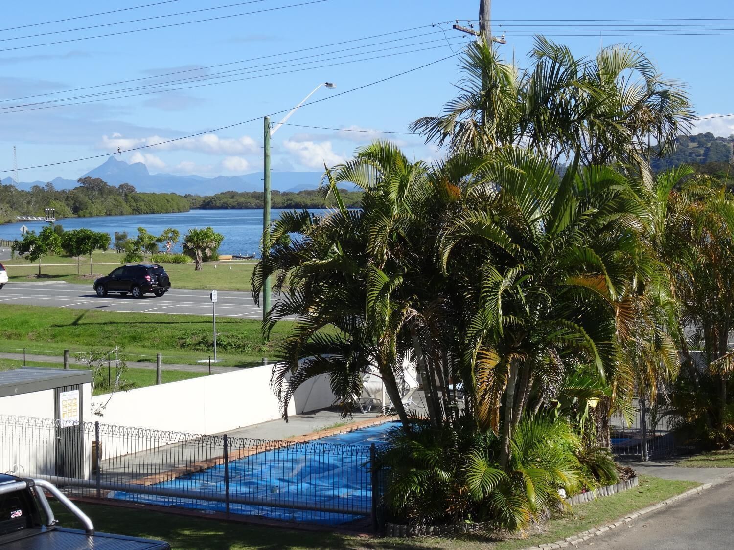 Área residencial com piscina, palmeiras e vista para um lago e montanhas.