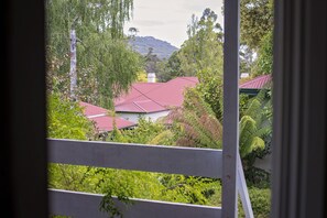 Vista de uma varanda com um edifício de telhado vermelho, cercado por vegetação exuberante e uma montanha ao fundo.