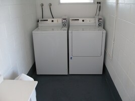 Uma lavanderia com duas máquinas de lavar brancas de carregamento frontal e uma pequena mesa.