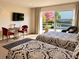 Quarto de hotel com cama, escrivaninha e cadeira, TV na parede e varanda com vista para árvores.