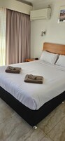Quarto de hotel com cama, duas toalhas, mesa de cabeceira, ar condicionado fixado na parede e janela com cortinas.