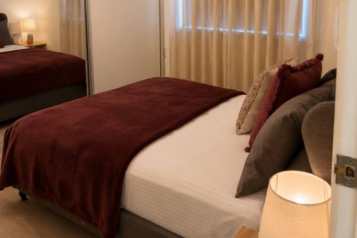 Quarto de hotel com cama, mesa de cabeceira com abajur, ventoinha no teto e janela com cortinas.