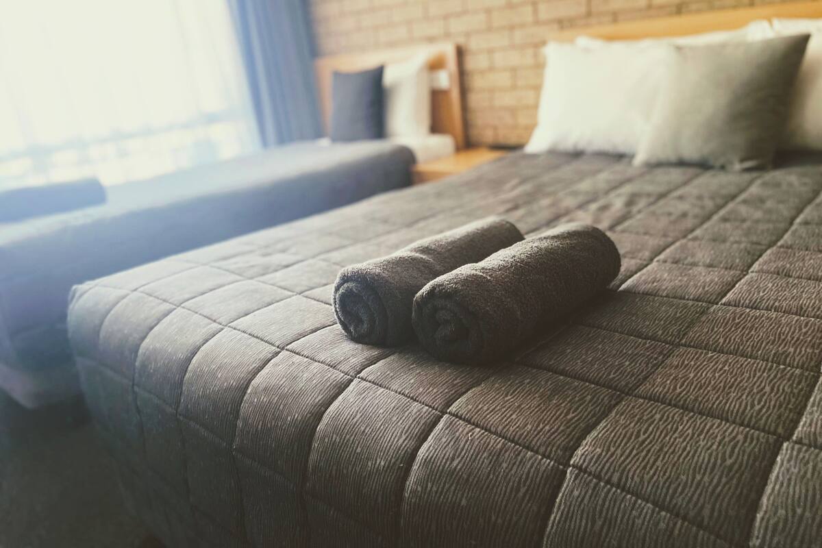 Cama bem arrumada com manta acolchoada e duas toalhas enroladas.