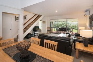 Uma sala de estar moderna com escada, área de jantar e pátio com mobiliário exterior.