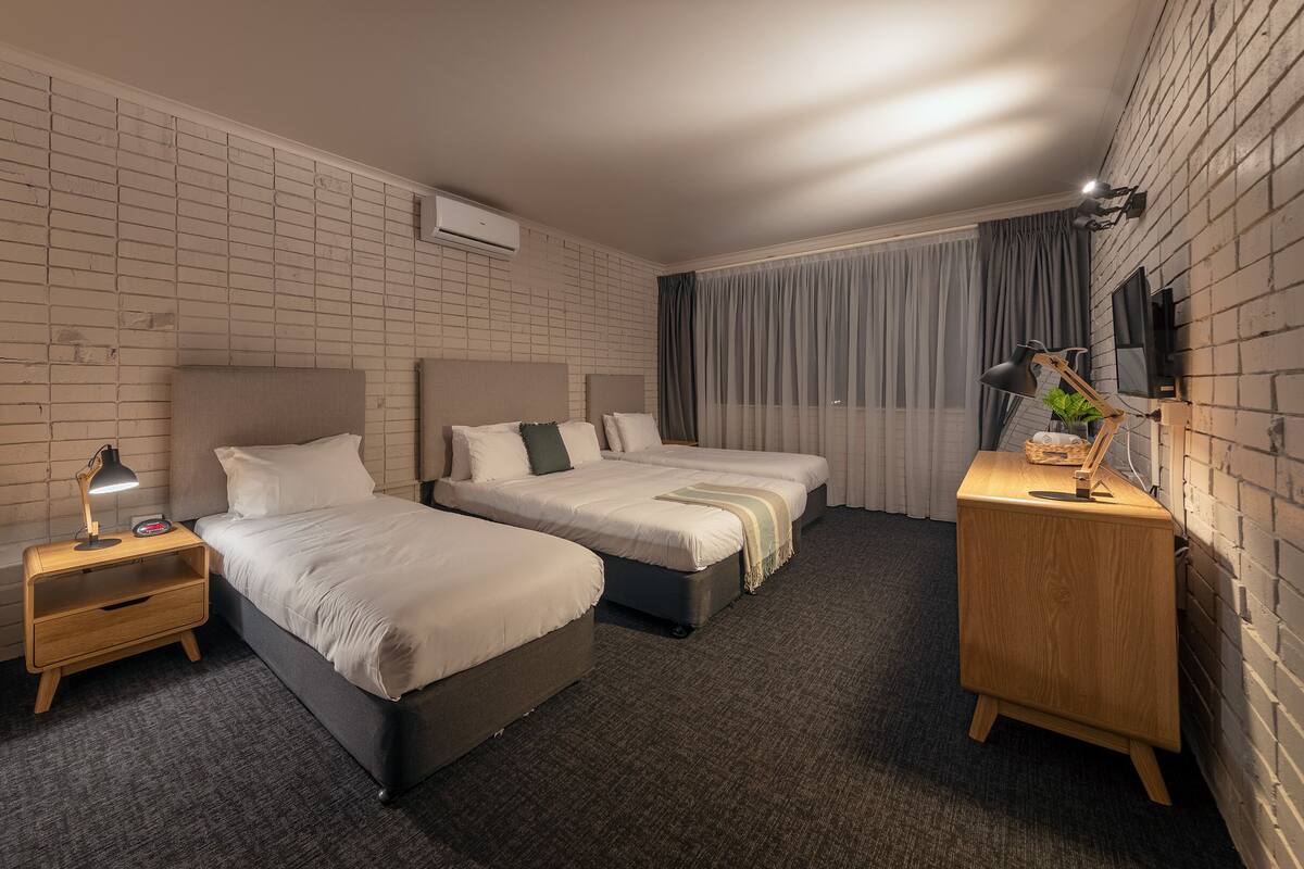 Quarto de hotel com duas camas, uma escrivaninha, uma luminária e uma televisão.