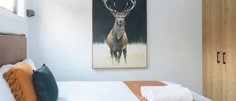 Quarto com cama, almofadas, manta, guarda-roupa de madeira e quadro com imagem de um veado.