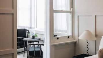Quarto de hotel com cama, mesa de cabeceira com abajur, cadeira e janela com cortinas.