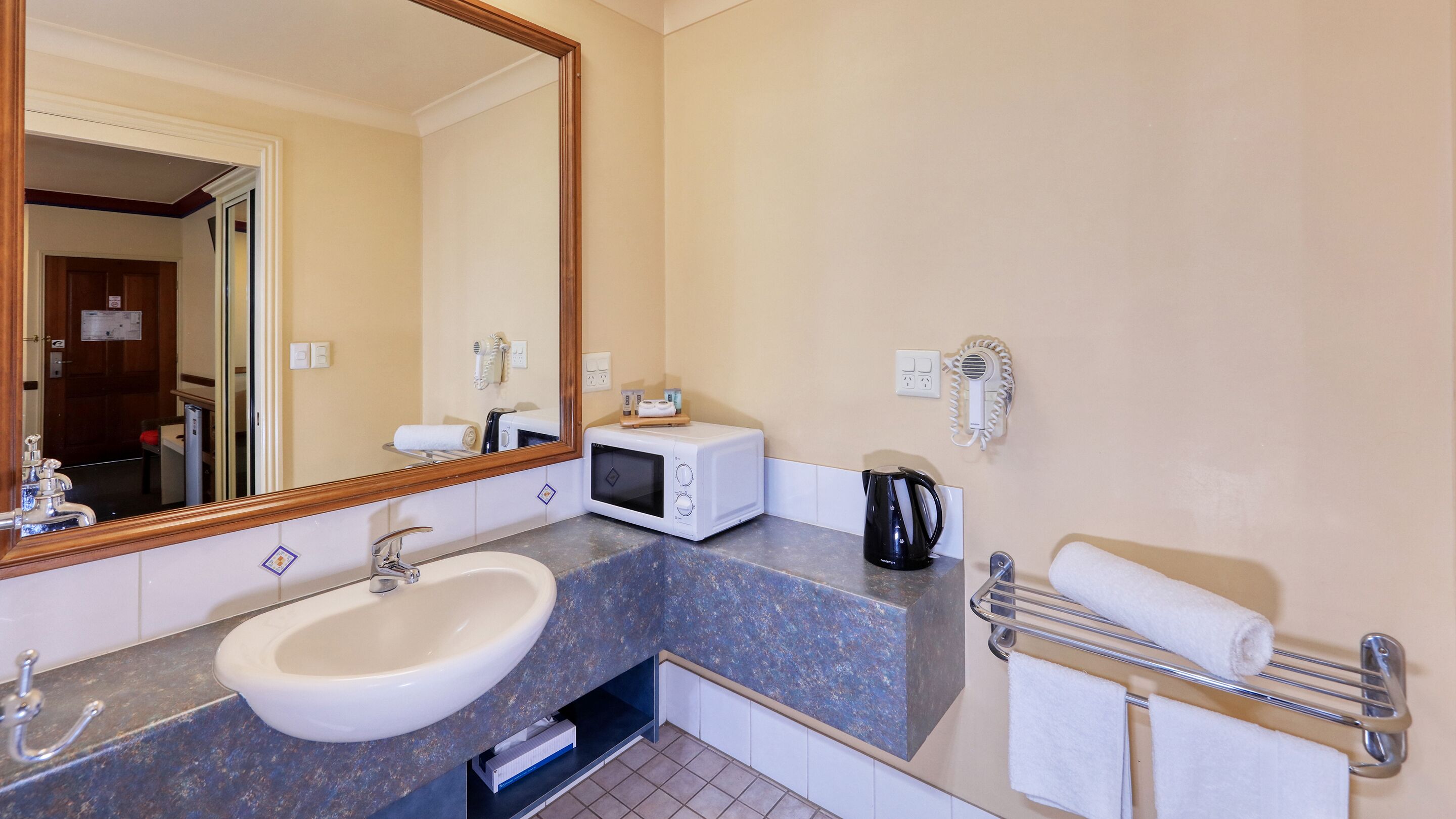 Casa de banho com lavatório, espelho, micro-ondas, secador de cabelo e um porta-toalhas.
