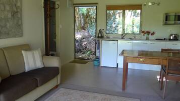 Uma sala de estar moderna com sofá, mesa de jantar e área de cozinha com geladeira e pia.