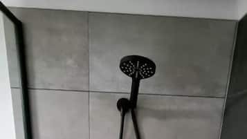 Chuveiro com chuveiro manual fixado na parede, painel de controle e porta-toalhas.