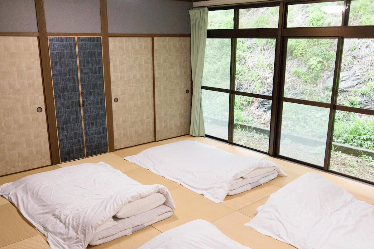 Quarto com piso de tatame, uma janela grande com vista para o verde e uma porta deslizante com padrão texturizado.