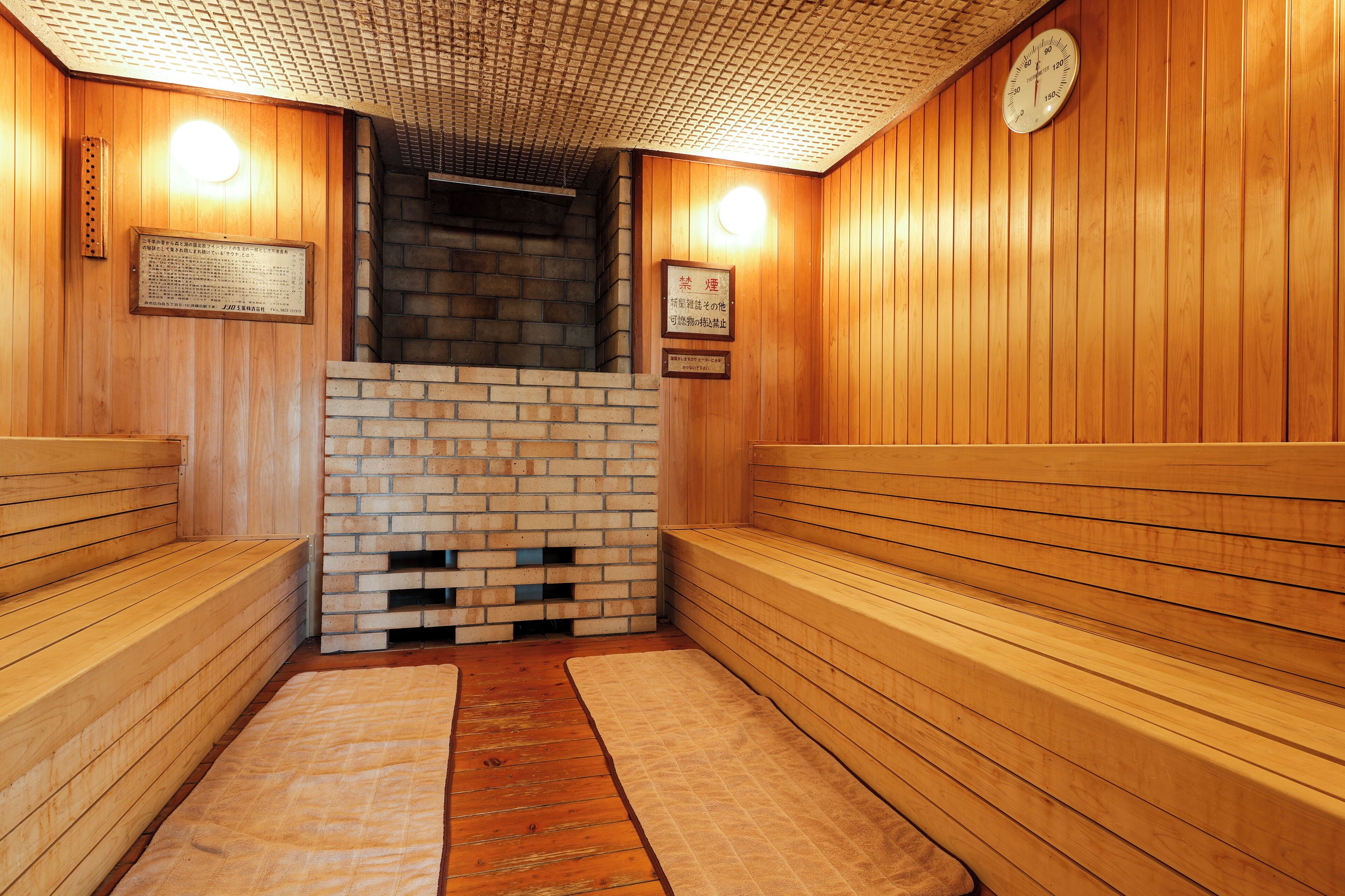 Uma sauna com bancos de madeira, parede de tijolos e um relógio na parede.