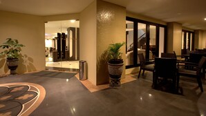 Um hall com balcão de recepção, plantas em vasos, escada e área de estar.