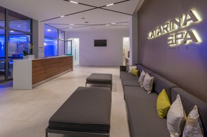 Interior moderno de spa, com balcão de recepção, área de estar e parede com marca do spa iluminada.