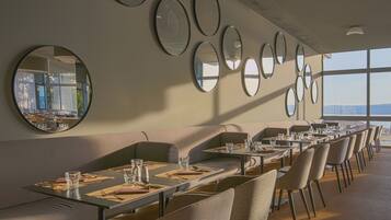 Um restaurante com um balcão comprido, vários espelhos redondos na parede e vista para a cidade através de grandes janelas.