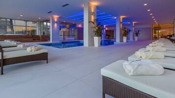 Espaço moderno de piscina interna com cadeiras de descanso e uma grande janela.
