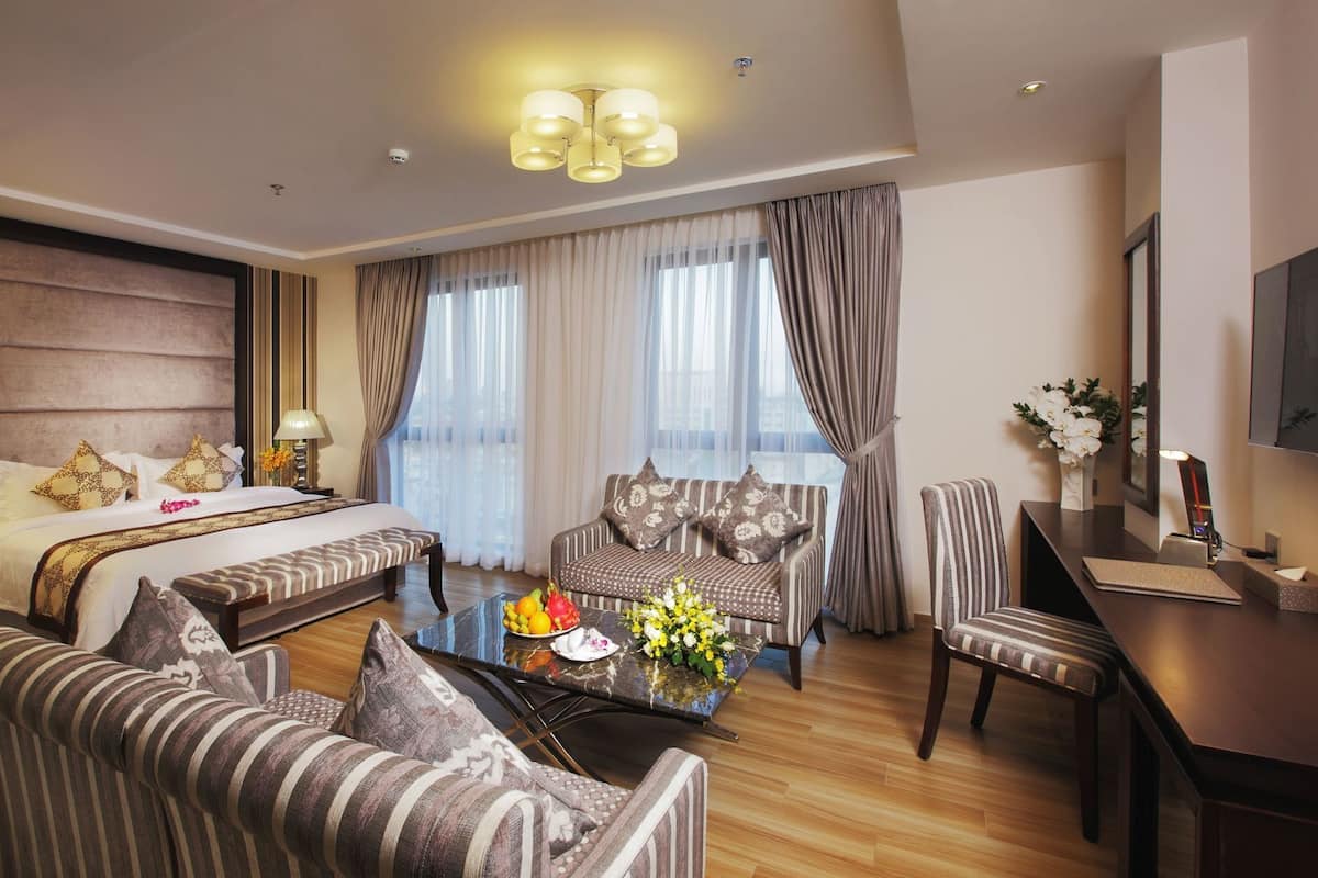 Quarto de hotel com uma cama grande, dois sofás, uma mesa de centro, uma escrivaninha e uma televisão.