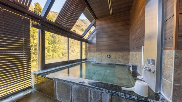 Uma área de spa com hidromassagem, paredes de pedra e grandes janelas com vista para uma colina.