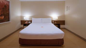 Cama bem arrumada em quarto de hotel com vista para a cidade, duas luminárias de cabeceira e mesa de cabeceira com telefone e uma mesinha.