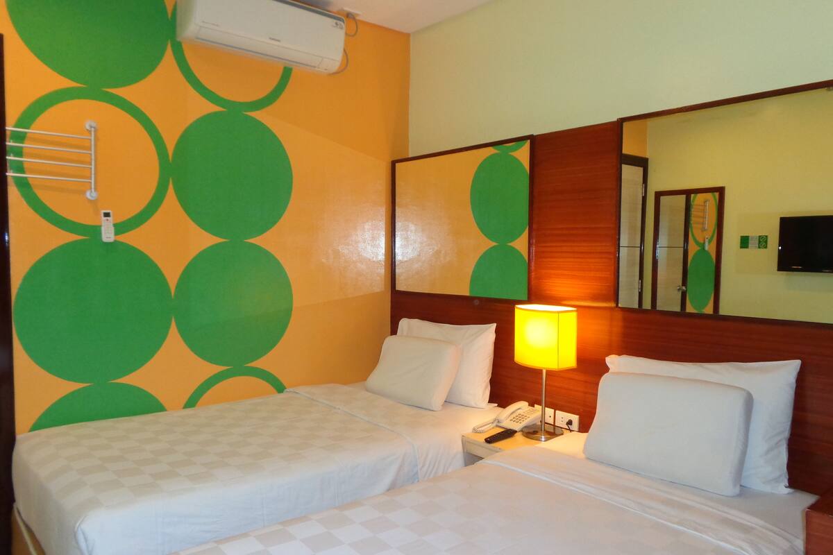 Quarto de hotel com duas camas, abajur, telefone e ar condicionado fixado na parede.