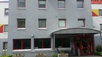 Um motel com fachada cinzenta, várias janelas e entrada vermelha.