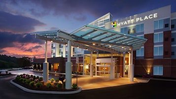 Entrada de um hotel Hyatt Place, com galeria coberta, portas de vidro e fachada de tijolos.