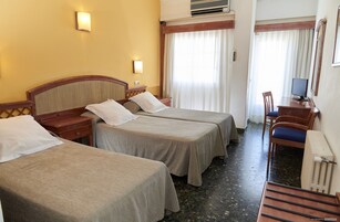 Quarto de hotel com duas camas individuais, uma escrivaninha com um computador, uma cadeira e um radiador.
