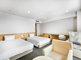 Quarto de hotel com duas camas, uma escrivaninha, uma cadeira e uma luminária.