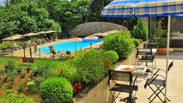 Um pátio externo com piscina, área de refeições e guarda-sóis.