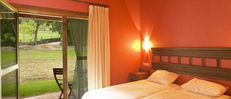 Quarto com uma cama grande, mesa de cabeceira, abajur e porta de vidro deslizante que dá para um alpendre.