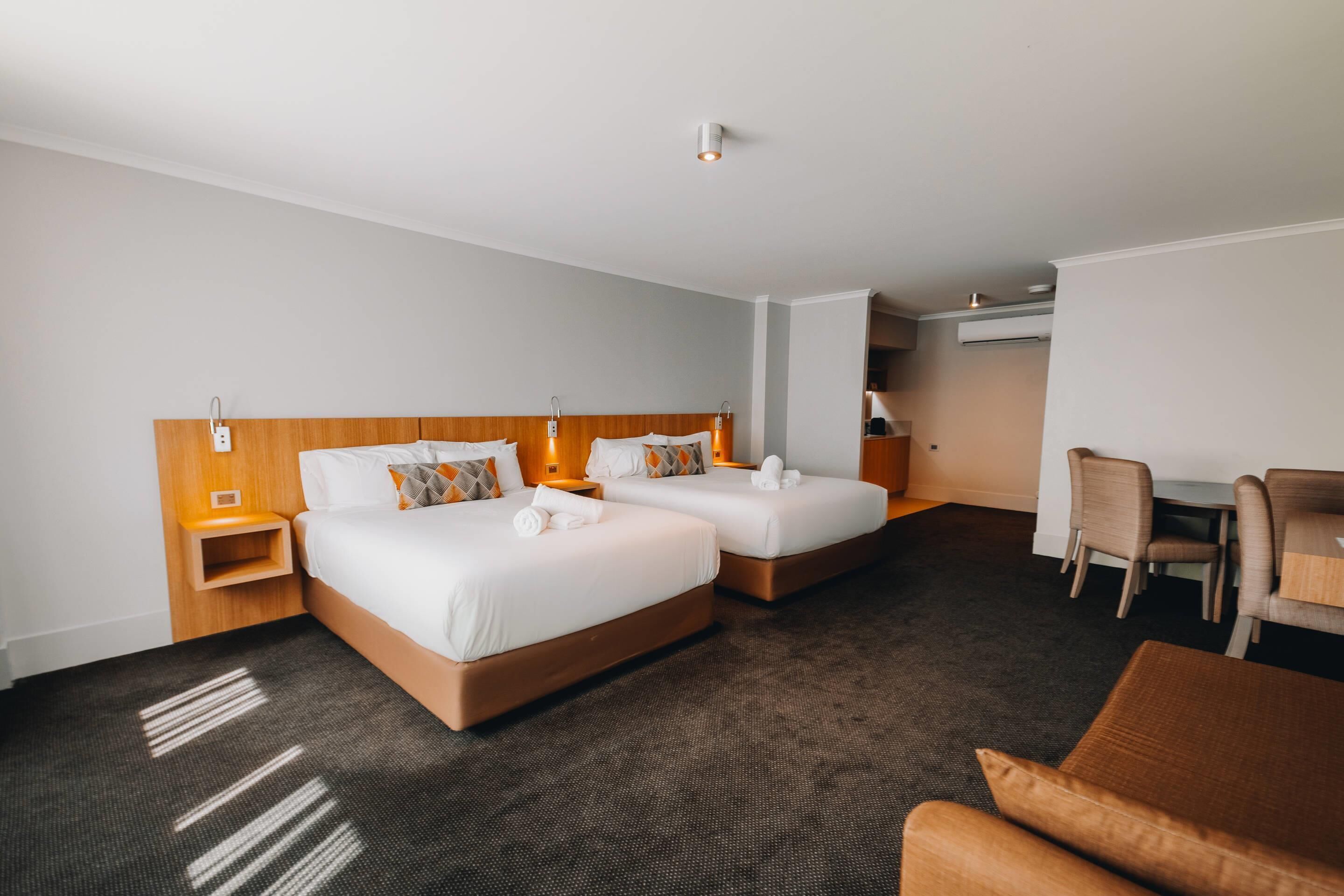 Quarto de hotel com duas camas, uma mesa e uma cadeira.