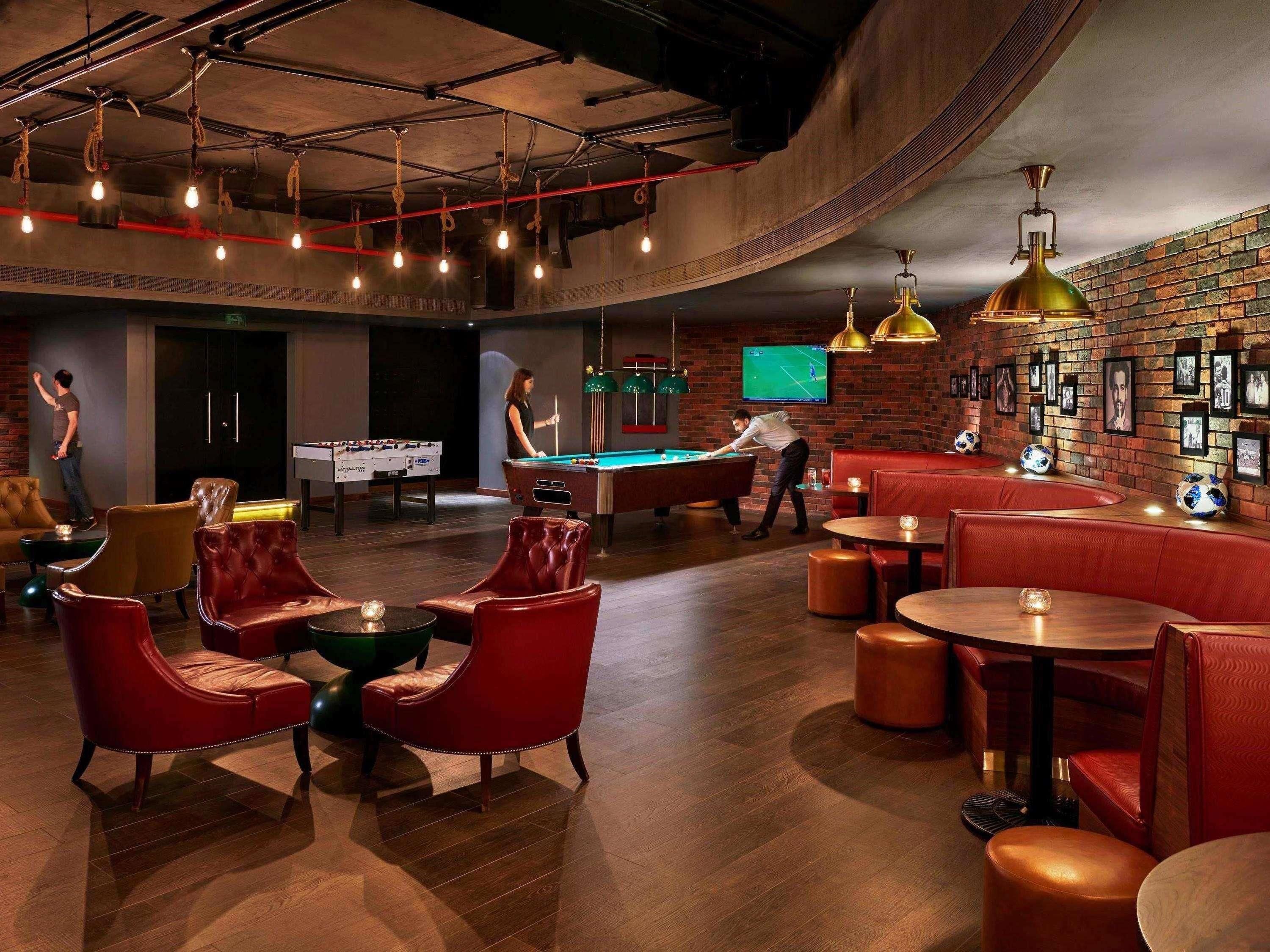 Uma área de bar com mesas de bilhar, assentos de couro vermelho e uma parede de tijolos com quadros.