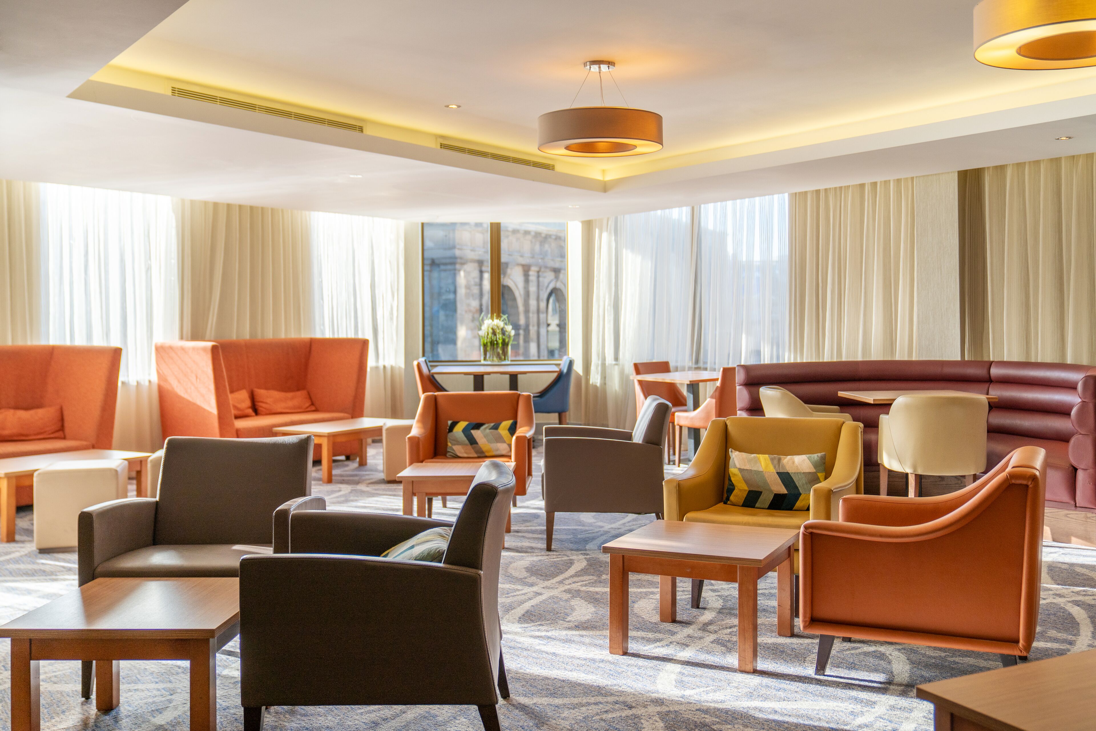 Um saguão de hotel com várias áreas de estar, incluindo sofás e poltronas, dispostas ao redor de mesas.