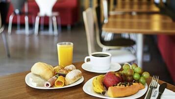 Uma mesa de café da manhã com pratos de doces, frutas e um copo de suco de laranja.