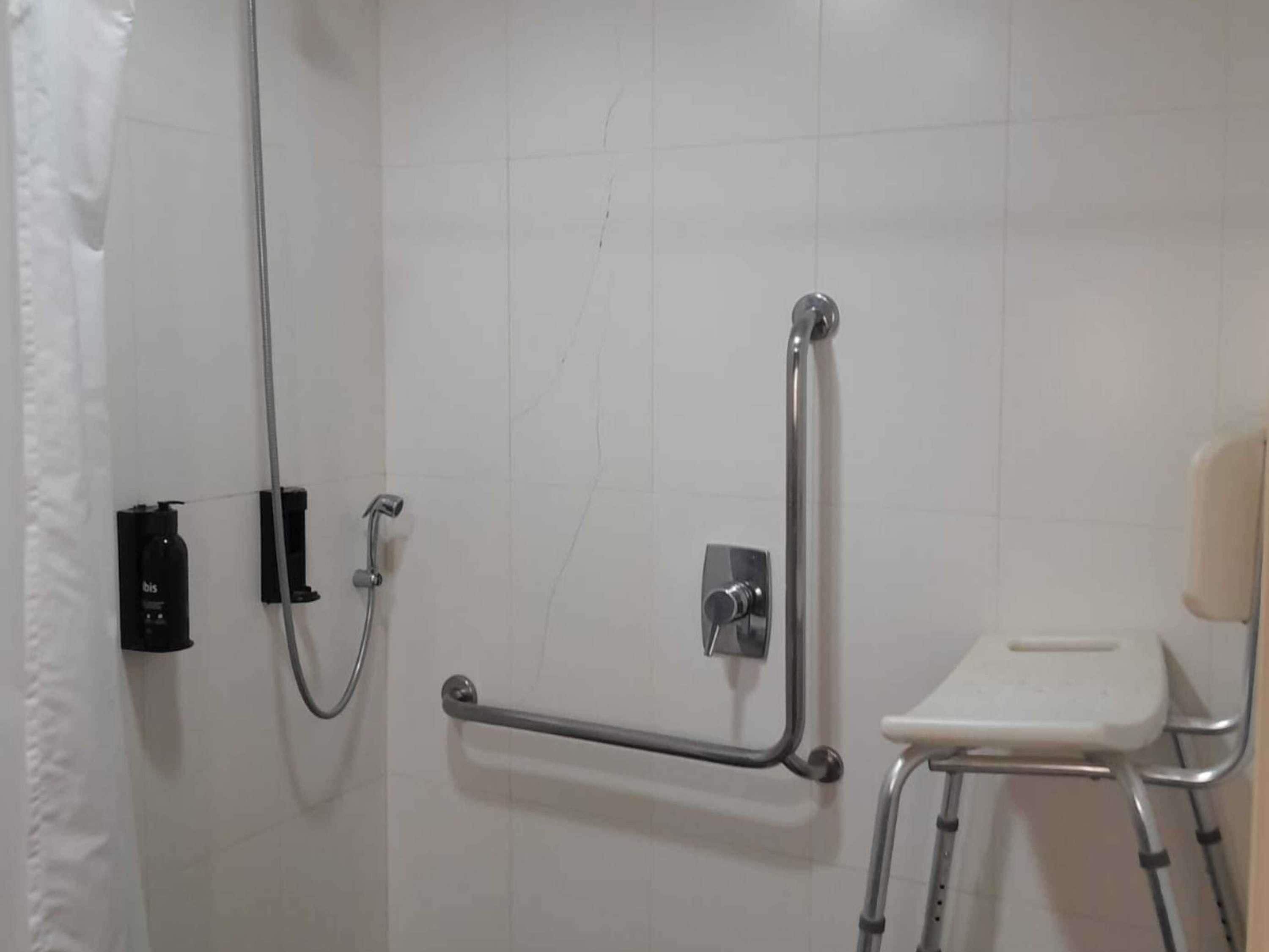 Casa de banho com chuveiro, barra de apoio e banco acessível para cadeiras de rodas.