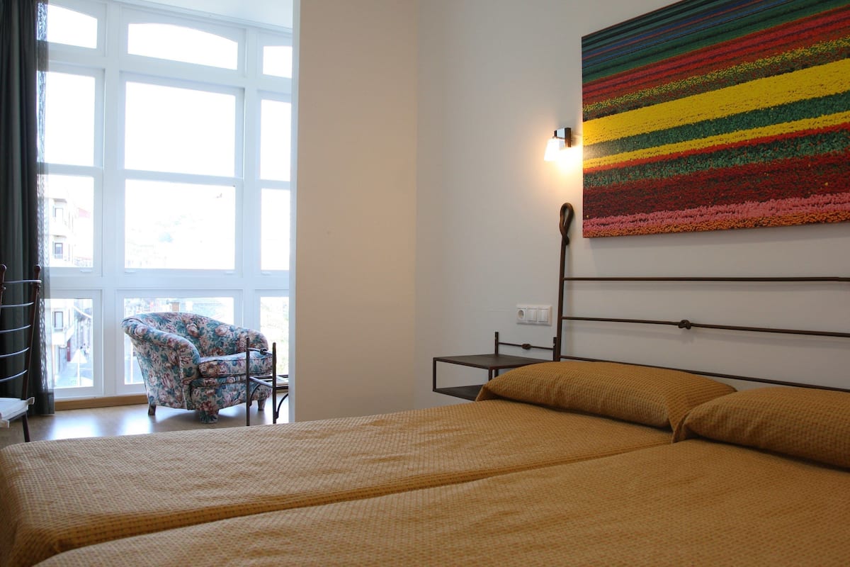 Quarto de hotel com uma cama grande, uma cadeira e uma pintura abstrata e colorida na parede.