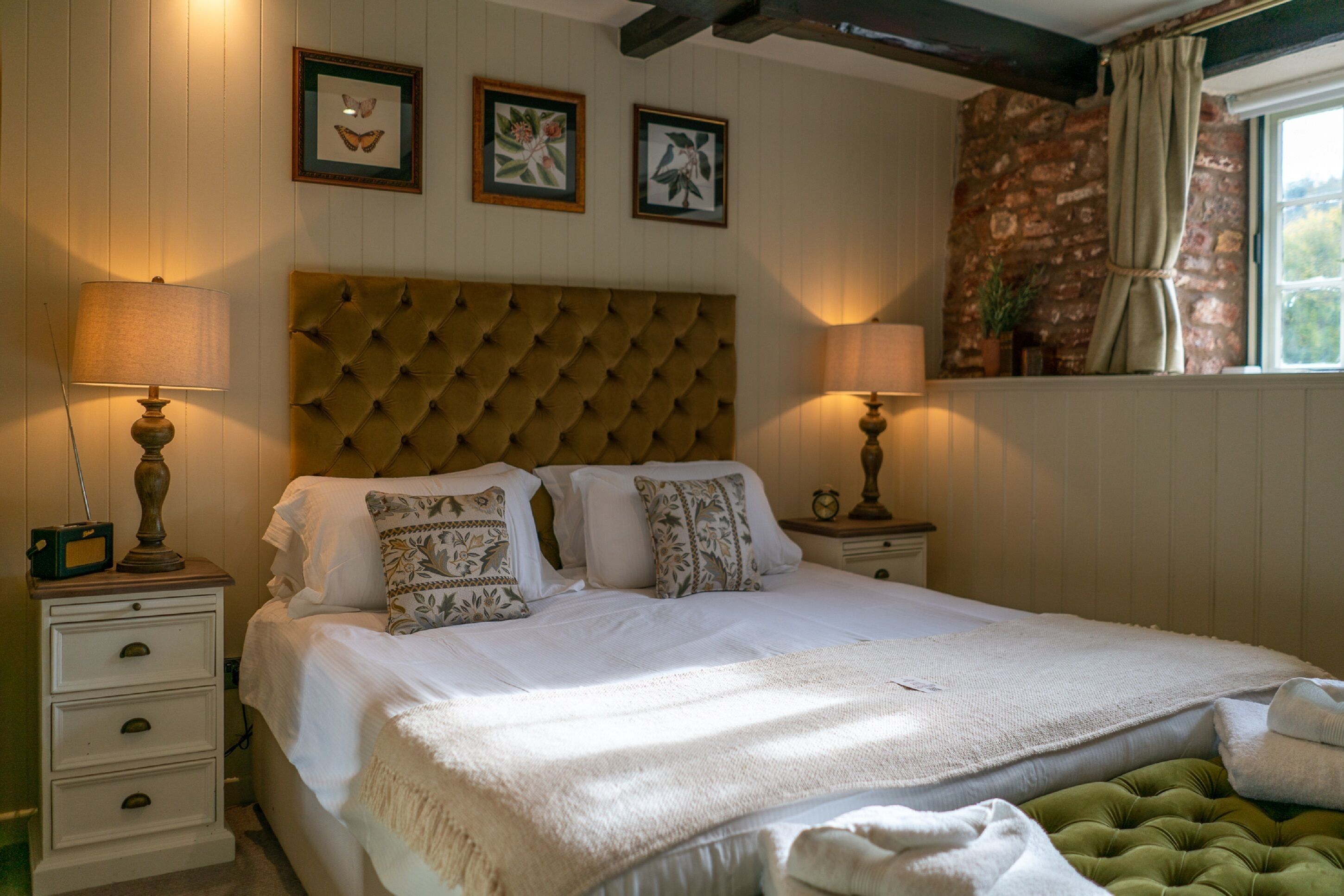 Quarto com uma cama grande, duas mesas de cabeceira com luminárias, um painel de cabeceira estofado verde e obras de arte emolduradas na parede.