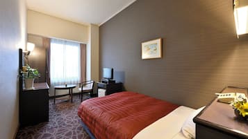 Quarto de hotel com cama, escrivaninha, cadeira, televisão e janela com cortinas.
