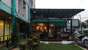 Um restaurante com mesas ao ar livre, toldo verde e placas com os dizeres 'CHILL' e 'REPEAT'.