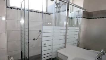 Casa de banho moderna com chuveiro em cabine de vidro, lavatório branco e espelho.