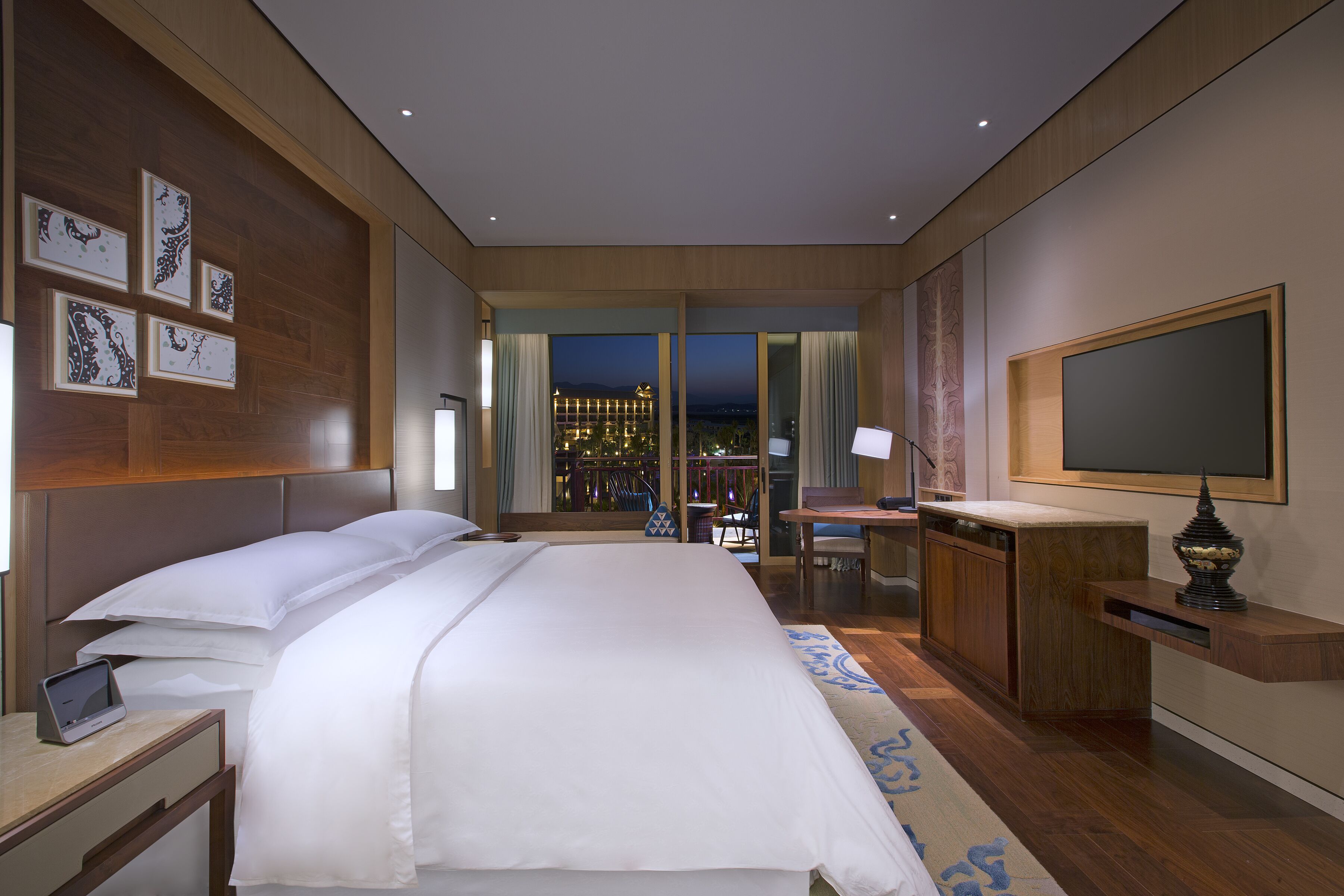 Quarto de hotel moderno com uma cama grande, uma escrivaninha e vista para a cidade à noite.