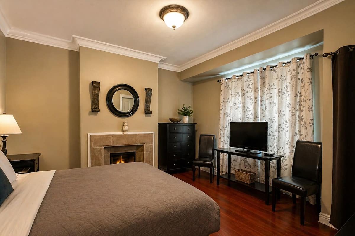 Quarto de hotel com uma cama grande, lareira, televisão e secretária com cadeiras.