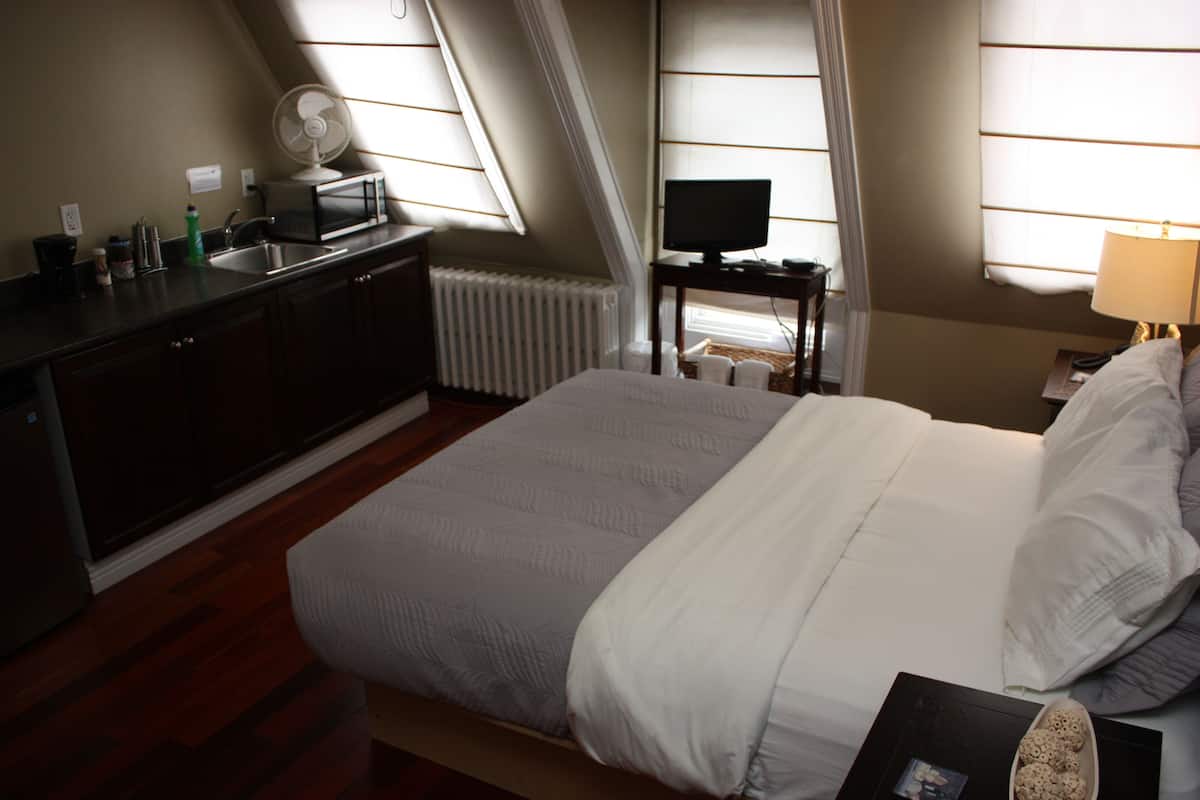 Um quarto com uma cama, uma escrivaninha, uma televisão e uma janela com cortinas.