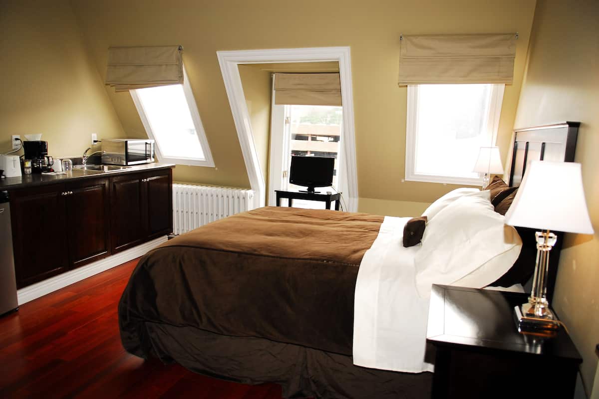 Quarto com cama, mesa de cabeceira, abajur, televisão e cozinha compacta.