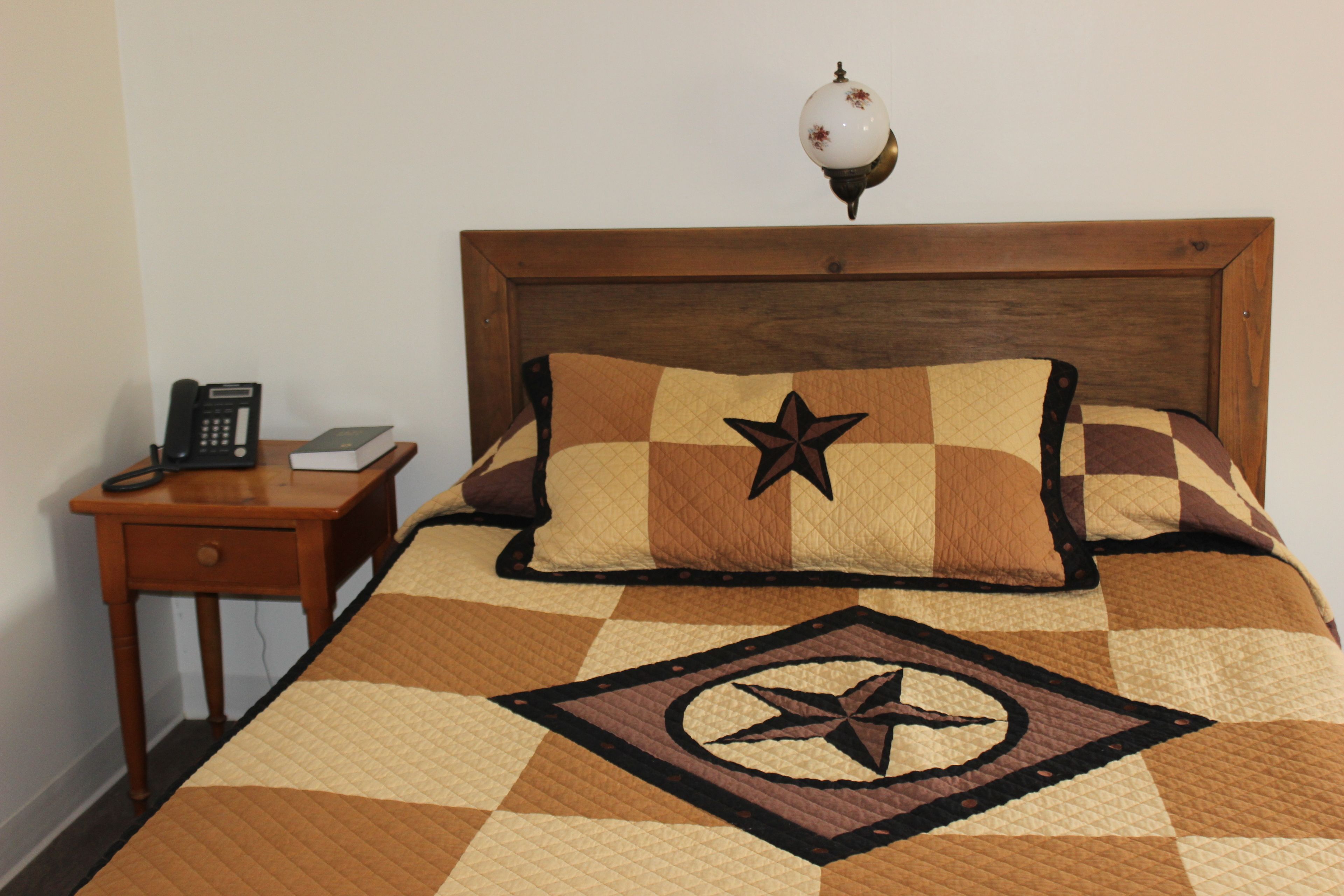 Uma cama bem arrumada com um espesso colcha acolchoado com padrão de estrelas, cabeceira de madeira e abajur.