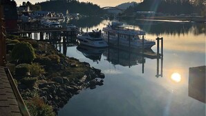 Uma marina com barcos atracados, uma ponte ao fundo e uma superfície aquática calma refletindo o céu.