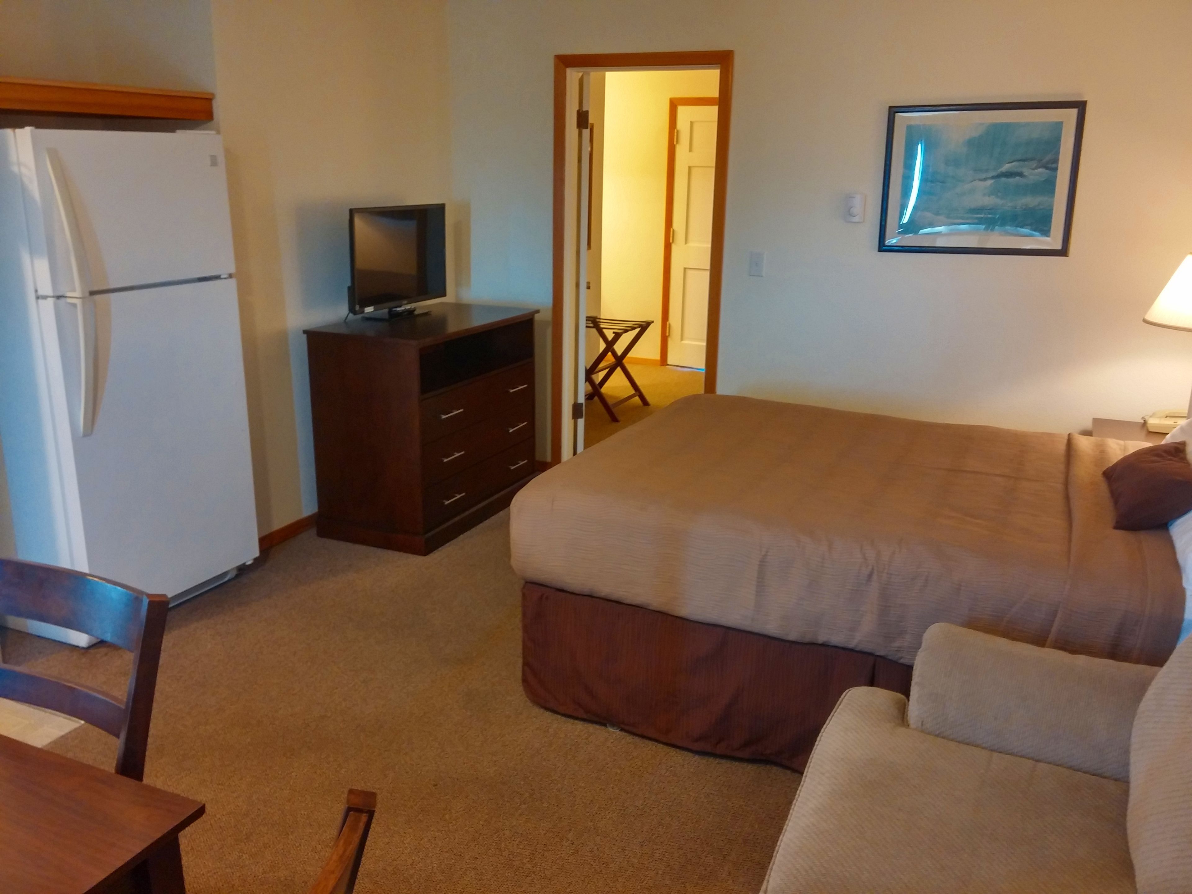 Quarto com cama, cômoda, televisão, escrivaninha e cadeira.