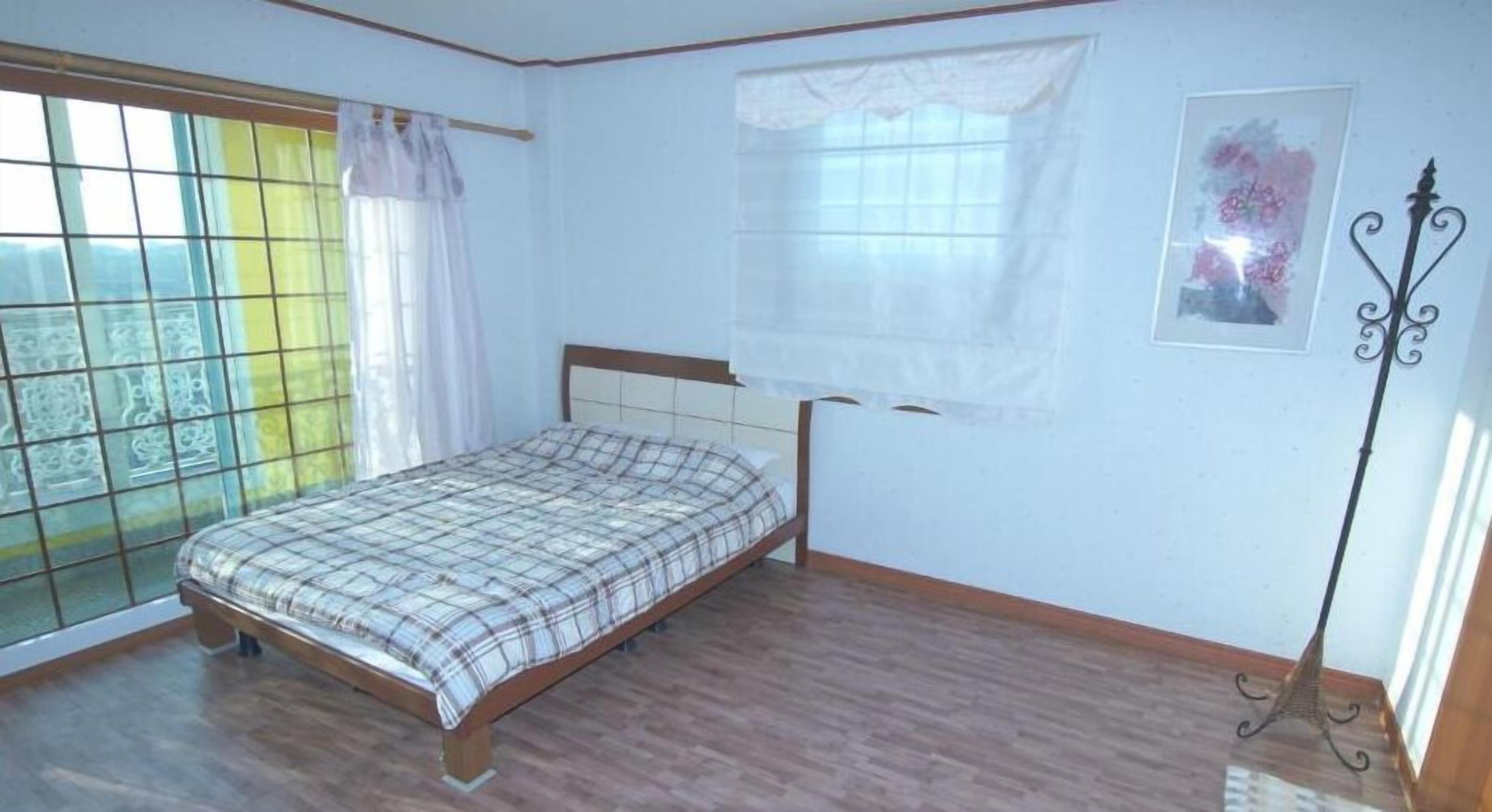 Um quarto com cama, janela com cortinas, quadro na parede e abajur.