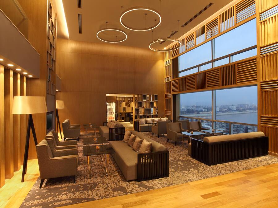 Interior moderno com sofá, poltronas, mesa de centro e uma grande janela com vista para a cidade.